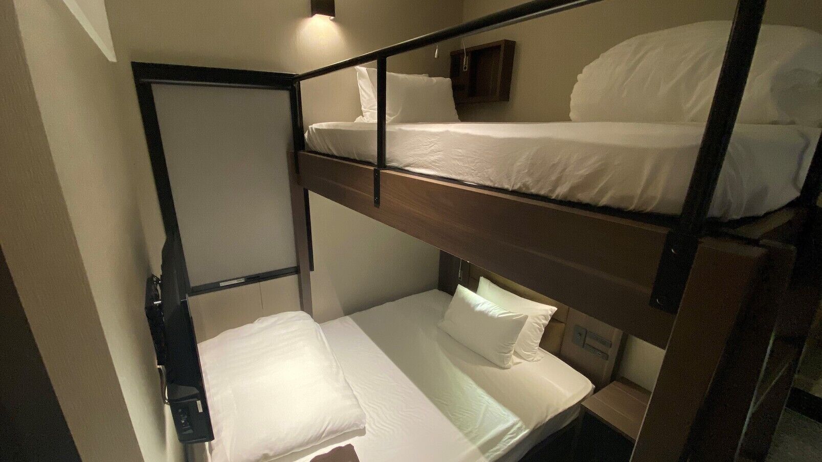 Quarto com beliche de madeira, roupa de cama branca e um pequeno armário.