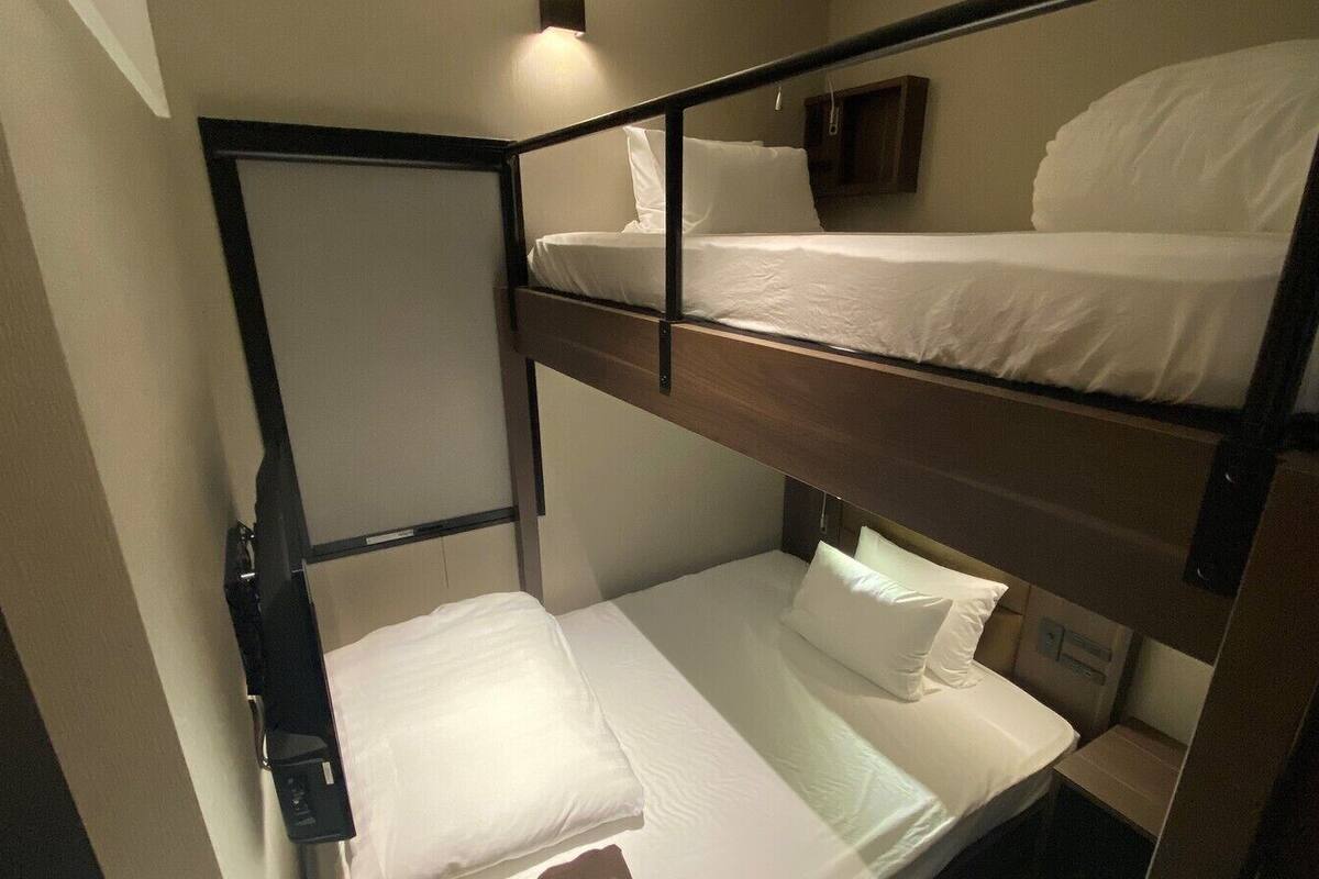 Quarto com beliche de madeira, roupa de cama branca e um pequeno armário.