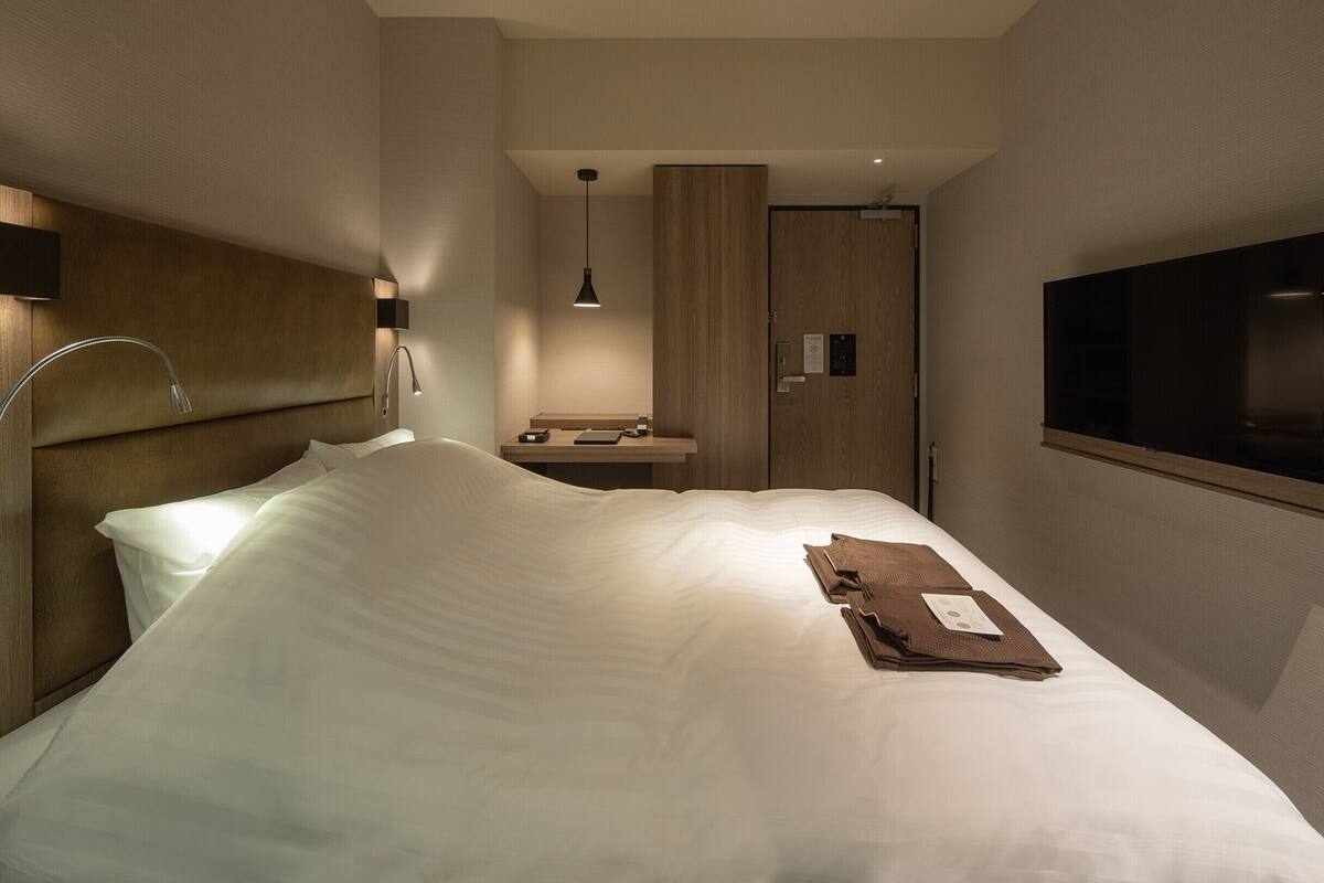 Quarto de hotel com uma cama grande, mesa de cabeceira, televisão e banheiro com espelho e pia.
