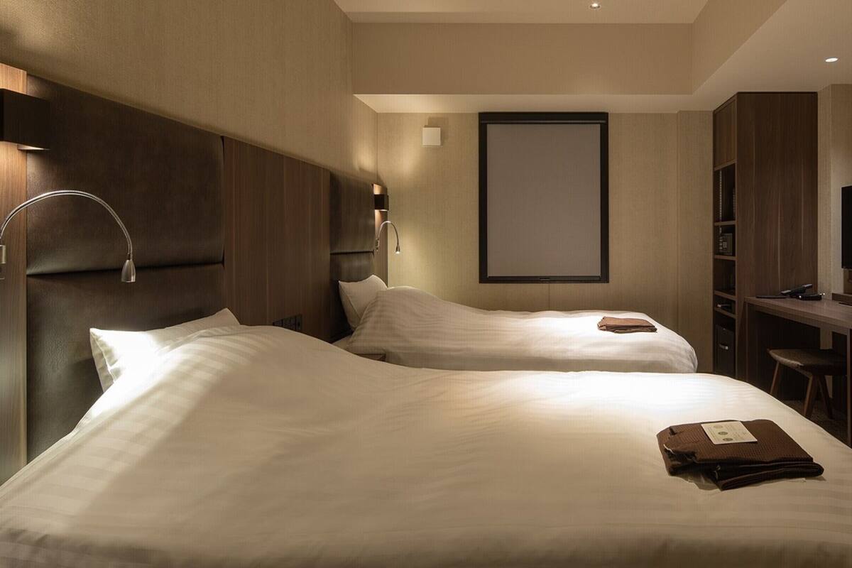 Quarto de hotel com duas camas, uma escrivaninha, uma televisão e um guarda-roupa.