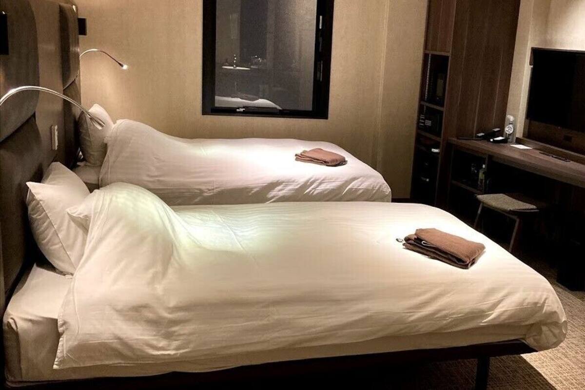 Quarto de hotel com duas camas, televisão e um pequeno espaço para sentar.