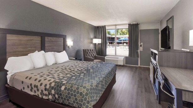 Quarto de hotel com uma cama grande, uma escrivaninha, uma cadeira, televisão e janela com cortinas.