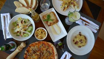 Uma mesa posta com diversos pratos, incluindo pizza, massa, salada e pão.