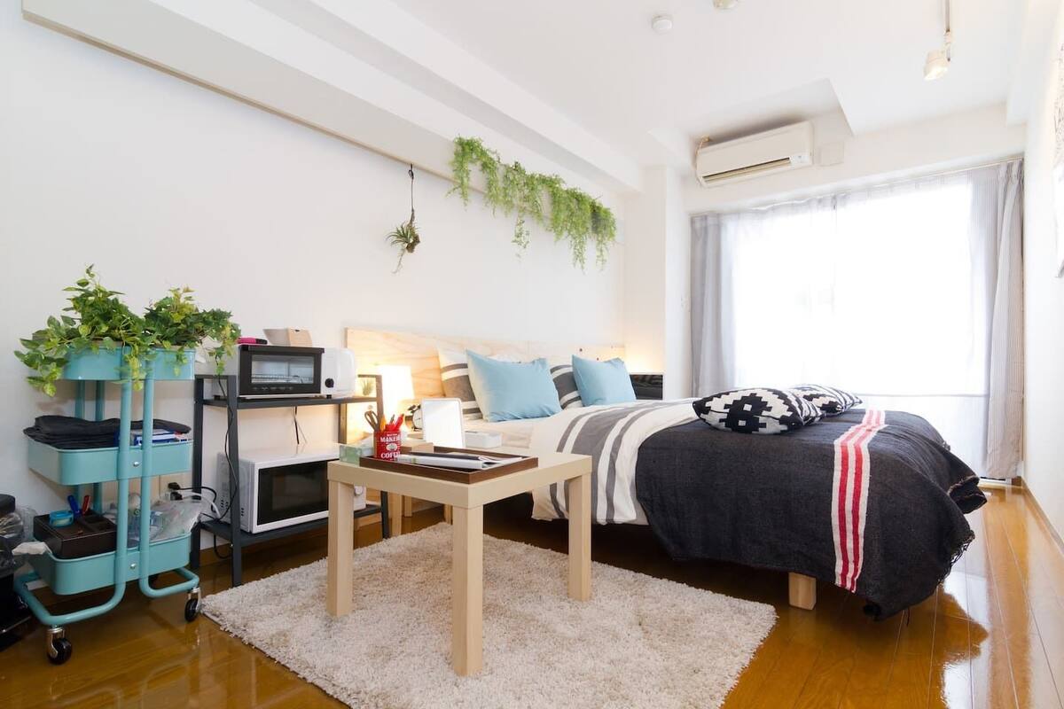 Quarto moderno com cama, escrivaninha, computador e um carrinho com planta.