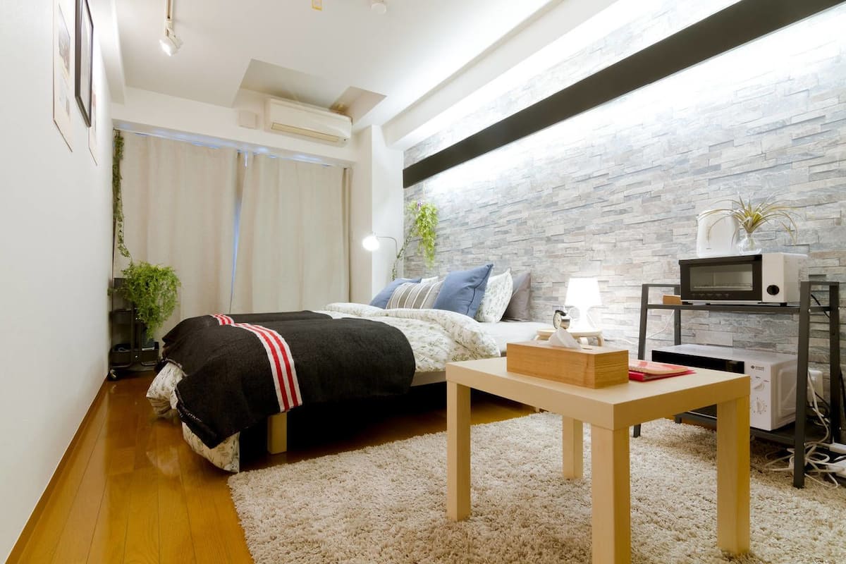Quarto moderno com cama, mesa de cabeceira e micro-ondas numa prateleira.