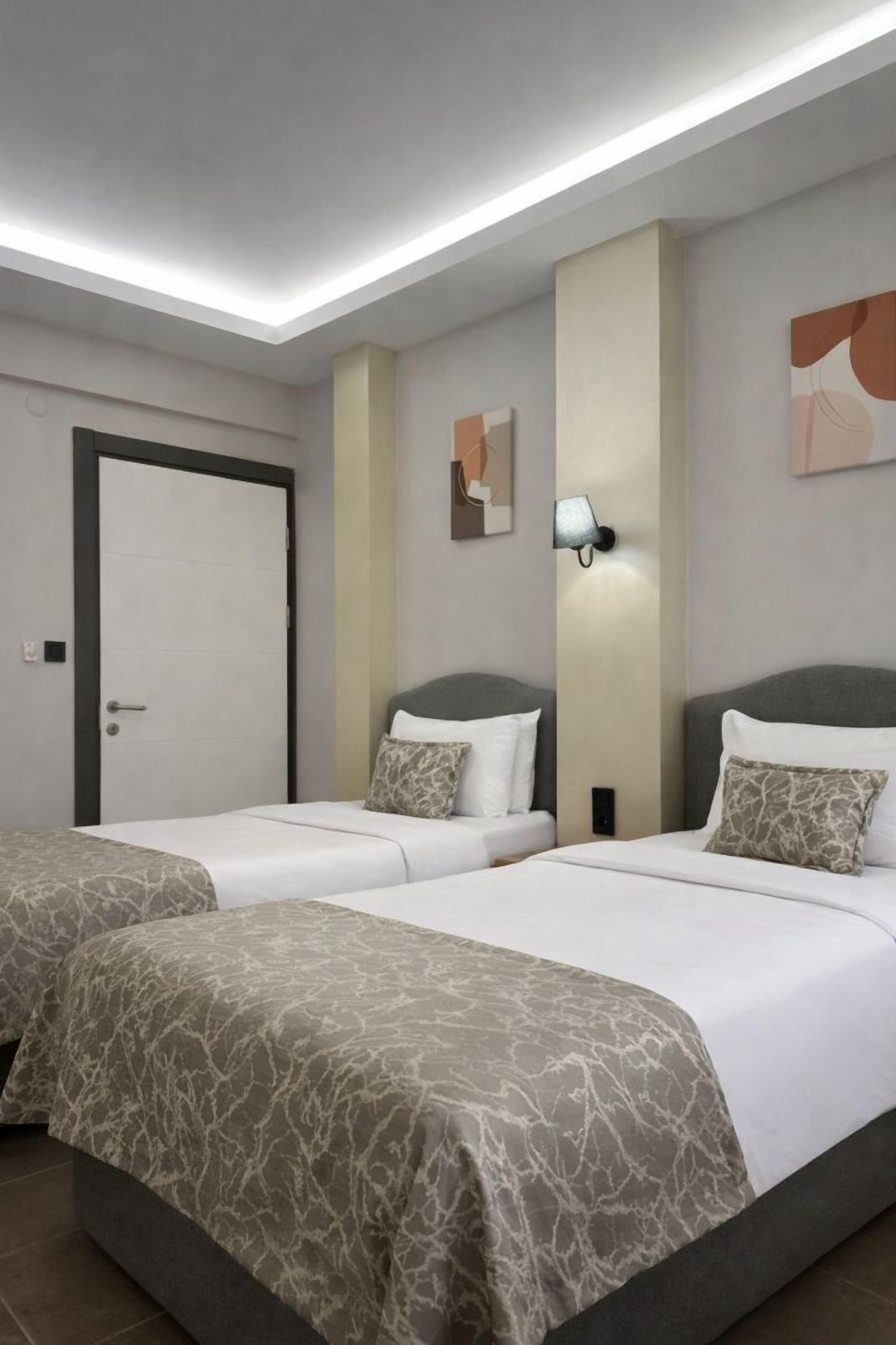 Quarto de hotel com duas camas, uma porta, uma luminária na parede e um quadro.