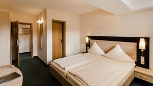 Quarto de hotel com cama, mesas de cabeceira, escrivaninha e porta.