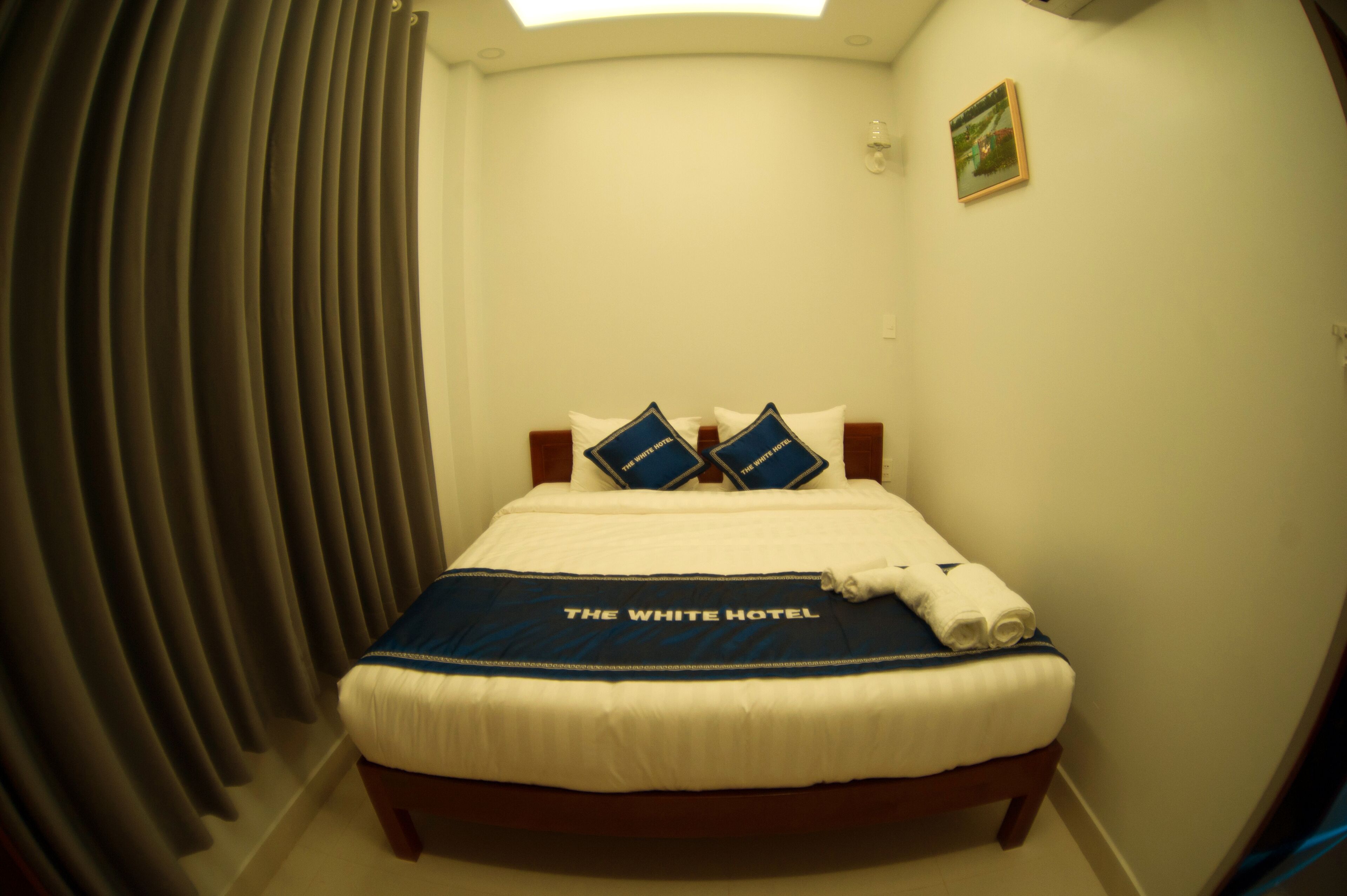 Quarto de hotel com cama, cortinas, um quadro na parede e uma toalha na cama.