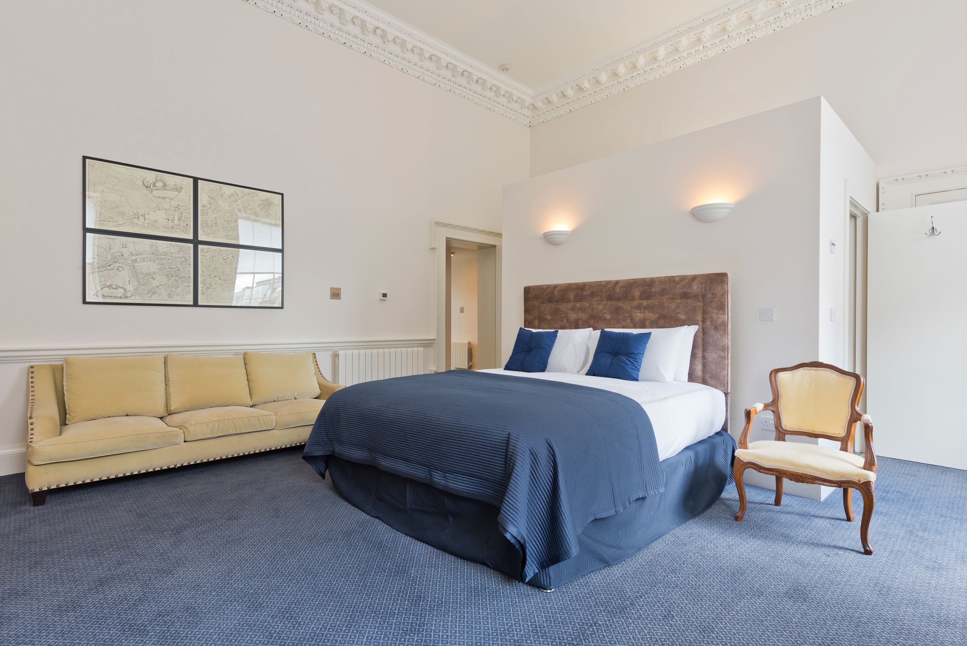 Quarto com cama grande, sofá, poltrona e luminária fixada na parede.