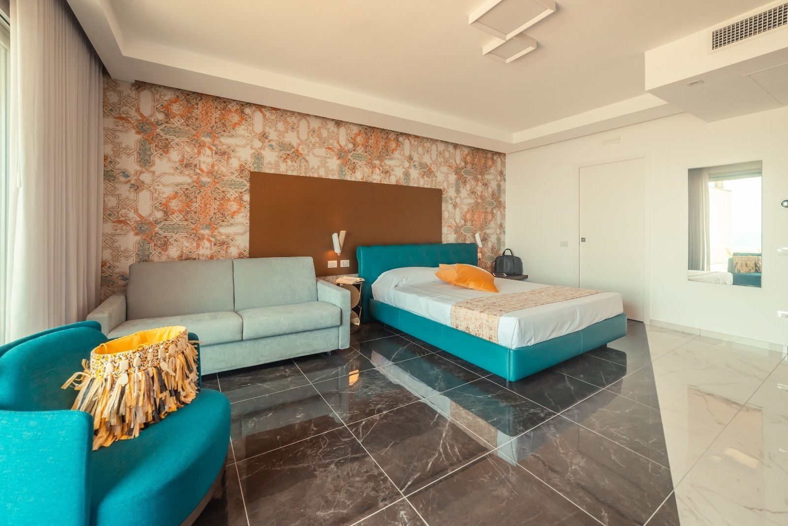 Quarto de hotel moderno com uma cama grande, um sofá e uma cadeira decorativa.