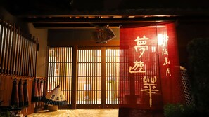 Entrada de um edifício japonês tradicional, com portas de correr e um rolo vermelho suspenso com caracteres dourados.