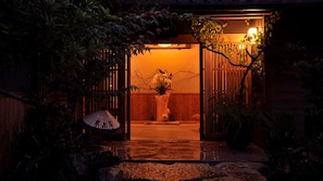 Uma entrada tradicional em estilo japonês, com portão de madeira, caminho de pedras e um vaso com planta.