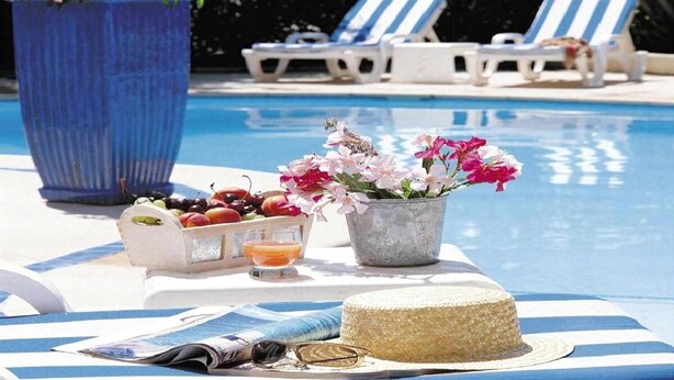 Área de piscina com espreguiçadeiras, uma cesta de frutas, bebida e chapéu.