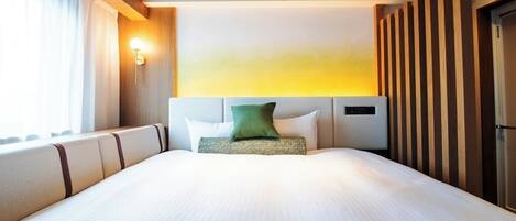 Quarto de hotel com uma cama grande, cabeceira com ar condicionado embutido, mesa de cabeceira e janela com cortinas.