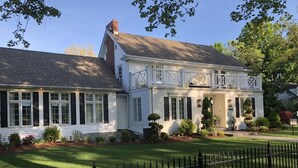 Uma casa de dois andares com varanda frontal, um pequeno jardim e cerca de metal preta.