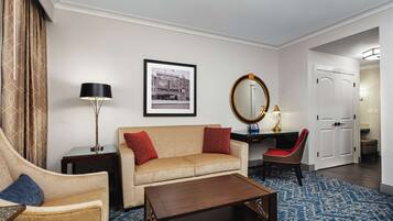 Quarto de hotel com sofá, poltrona, mesa de centro e um quadro emoldurado na parede.