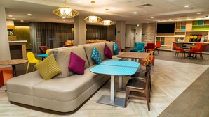 Um lobby moderno de hotel com área de estar, incluindo um sofá e mesas, área de bar com cadeiras e uma tela de televisão.
