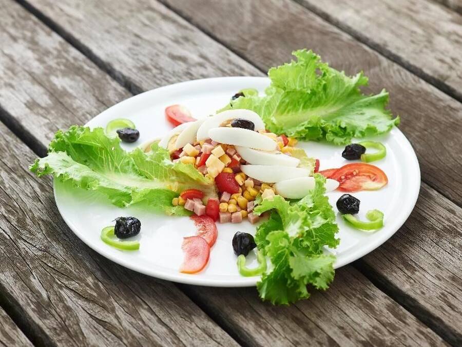 Prato branco com salada sobre mesa de madeira.