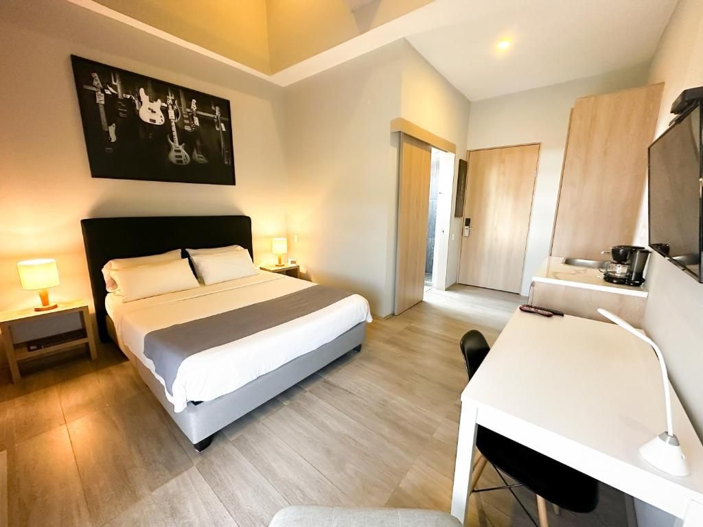 Quarto de hotel com cama, mesas de cabeceira, escrivaninha com cadeira, espelho e porta que dá para outro cômodo.