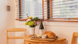 Uma mesa de madeira com um buquê de flores, uma garrafa de vinho, um pão e uma pequena tigela.