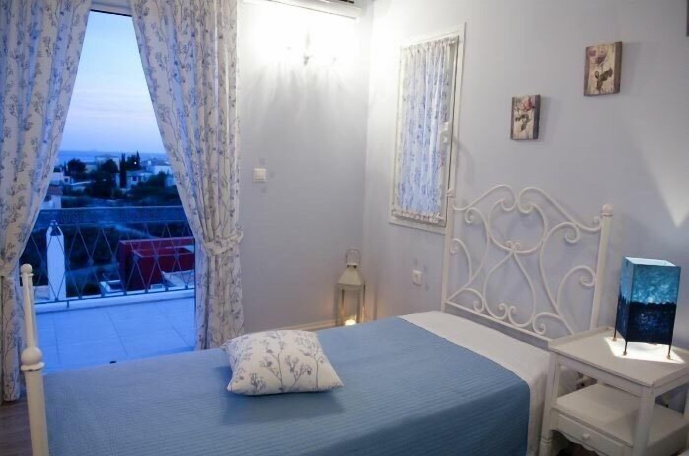 Quarto com cama, mesa de cabeceira, janela com cortinas e vista para o exterior.