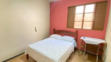 Quarto com cama, escrivaninha, cadeira, ventoinha no teto e janela com persianas.