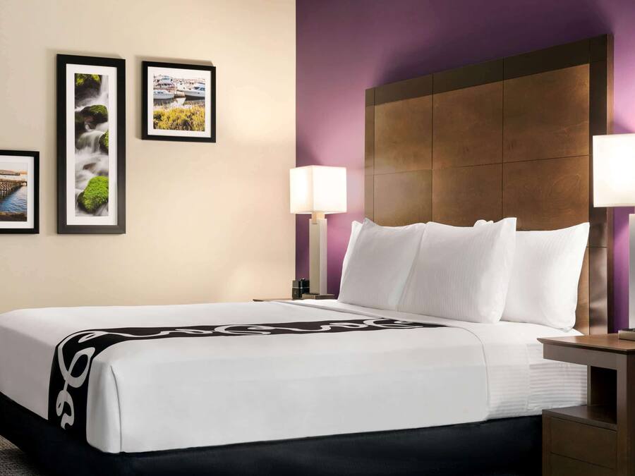 Quarto de hotel com uma cama grande, duas luminárias de cabeceira, uma cabeceira e três quadros na parede.