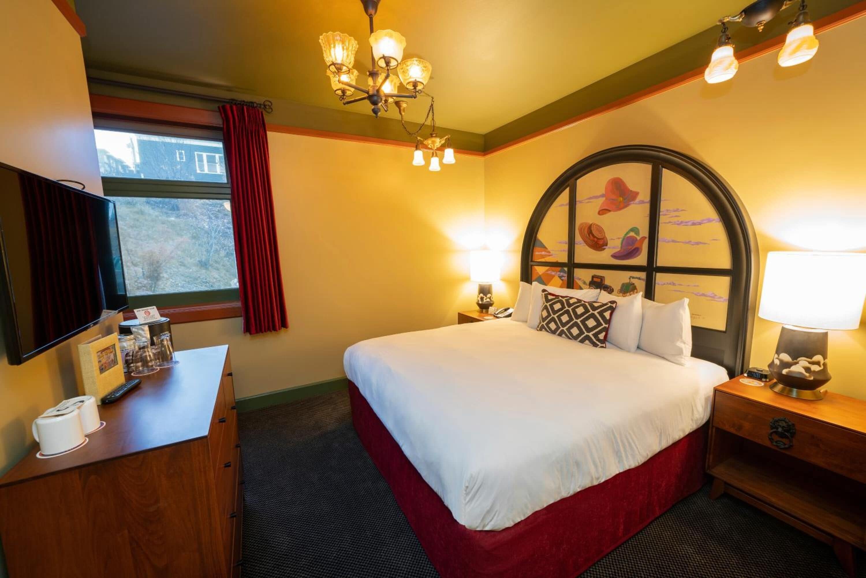 Quarto de hotel com uma cama grande, uma escrivaninha com telefone, uma televisão e uma janela com cortinas.