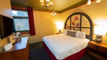 Quarto de hotel com uma cama grande, uma escrivaninha com telefone, uma televisão e uma janela com cortinas.