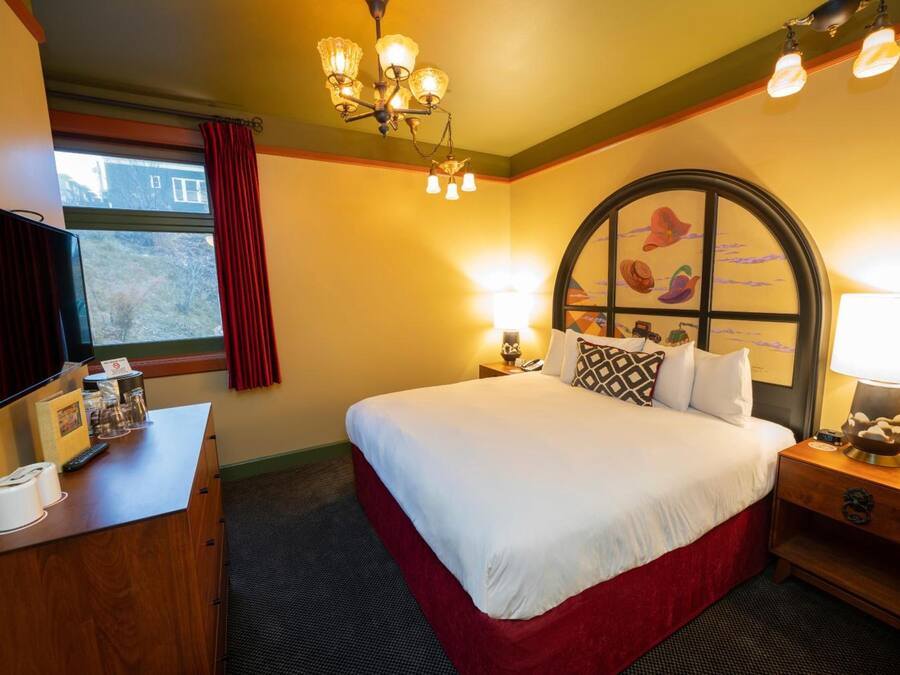Quarto de hotel com uma cama grande, uma escrivaninha com telefone, uma televisão e uma janela com cortinas.