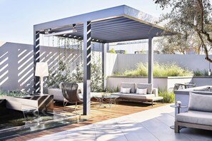 Um pátio moderno ao ar livre com pérgola, área de estar e um pequeno espelho d'água.
