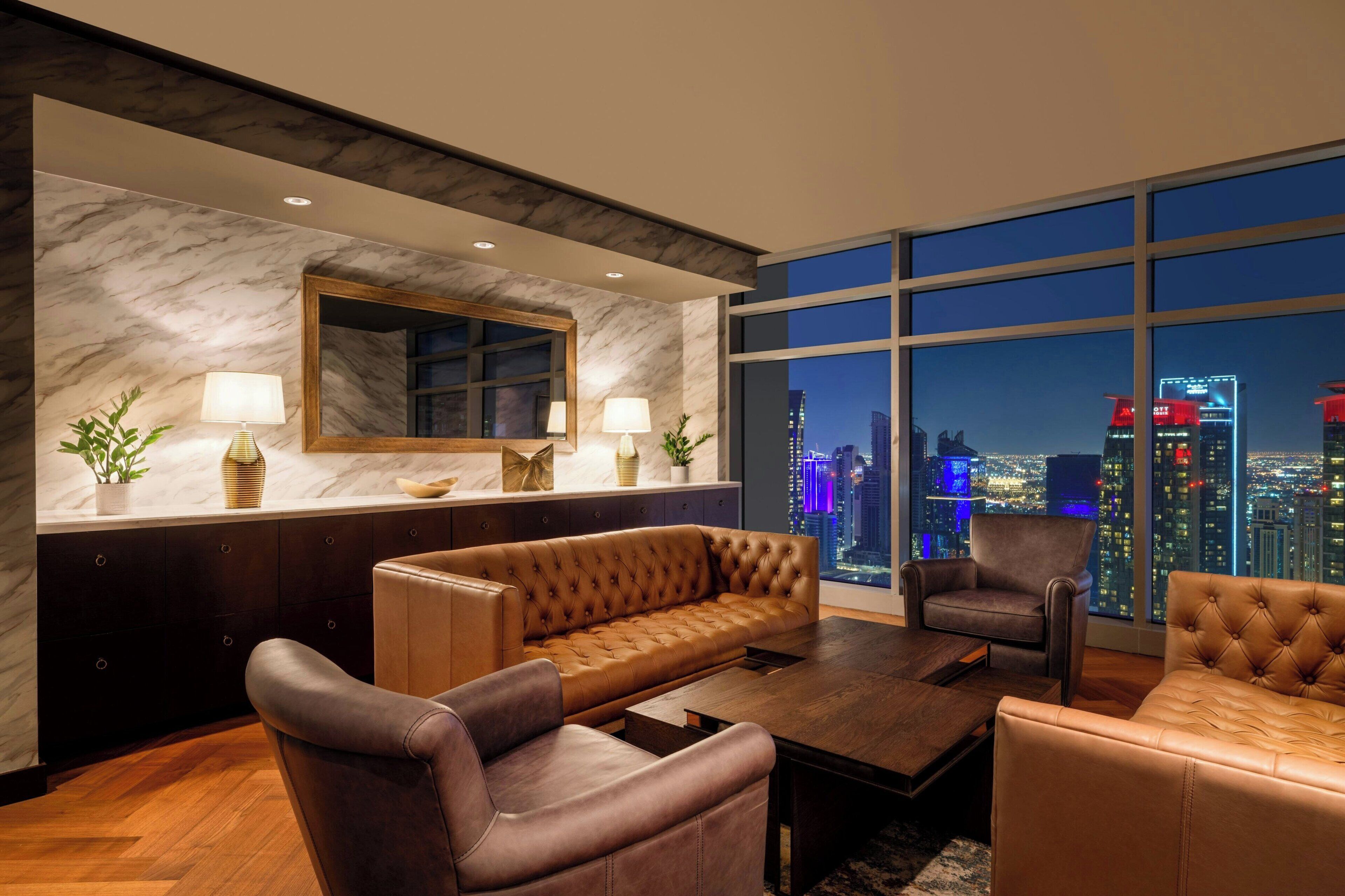 Uma sala de estar moderna com vista para a cidade, com um sofá, poltronas, uma mesa de centro e uma parede de destaque em mármore.