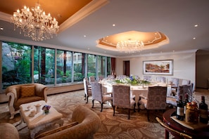 Uma sala de jantar com uma mesa grande posta para refeição, rodeada por cadeiras estofadas, e um candelabro acima.