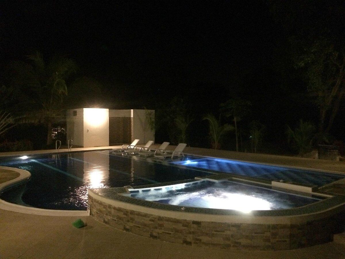 Piscina com espreguiçadeiras e um pequeno edifício ao fundo.