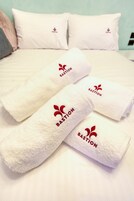 Cama bem arrumada com lençóis brancos e quatro toalhas dobradas com o logo 'Bastion'.