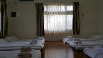 Quarto de hotel com quatro camas de solteiro dispostas em linha, piso de madeira e janela com cortinas leves.
