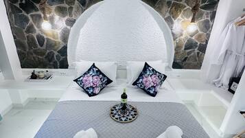Um spa moderno com parede de pedra, cama com almofadas florais, uma garrafa de vinho e toalhas no chão.