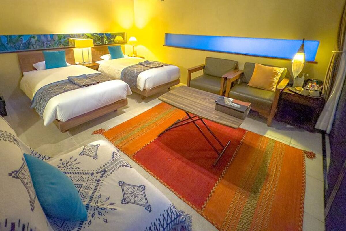 Quarto de hotel com duas camas, um sofá, uma mesa de centro e vista para o mar.