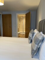 Quarto com cama, porta de madeira e banheiro visível através de uma porta aberta.