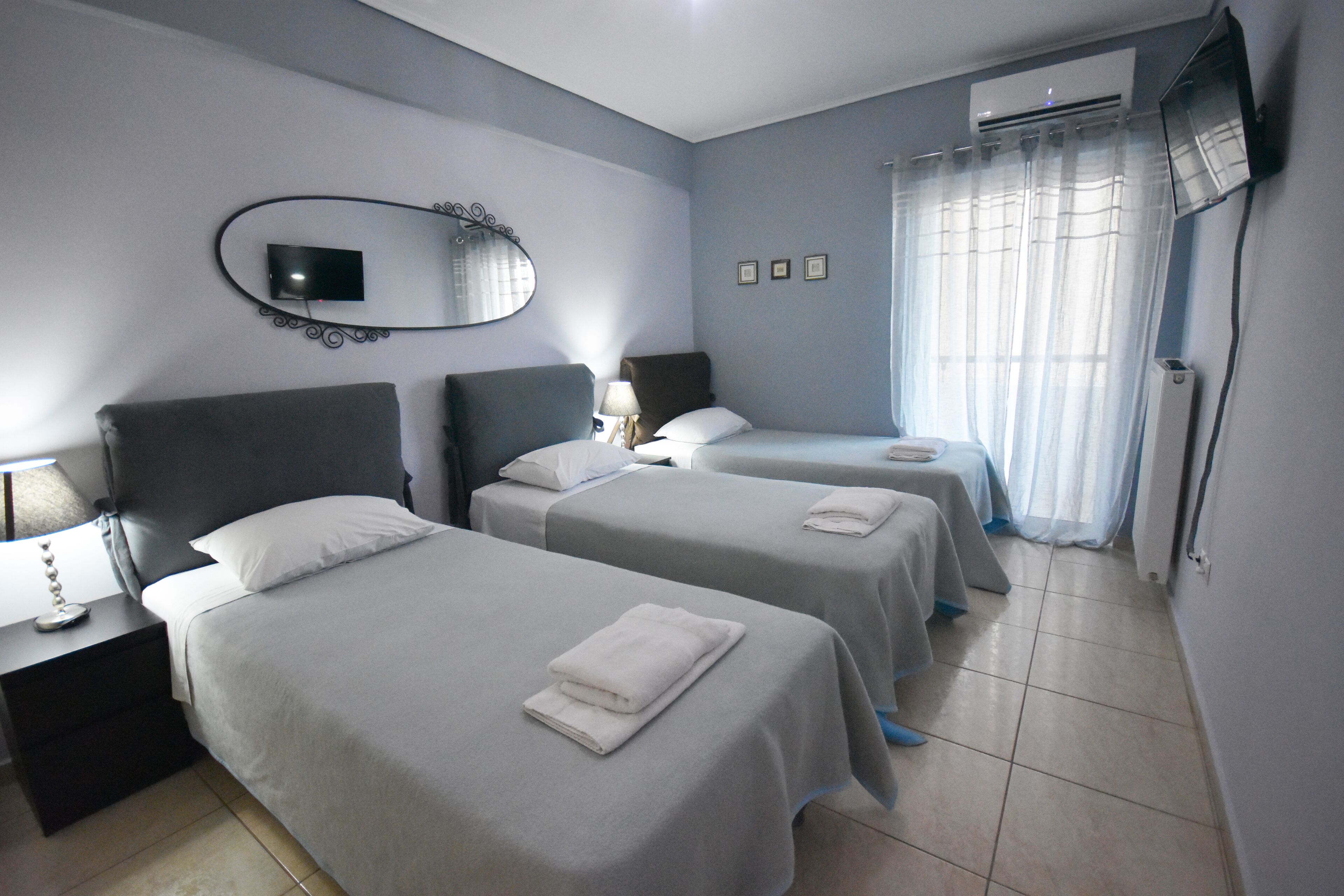 Quarto de hotel com duas camas, uma televisão presa à parede, um ar condicionado e uma janela com cortinas.
