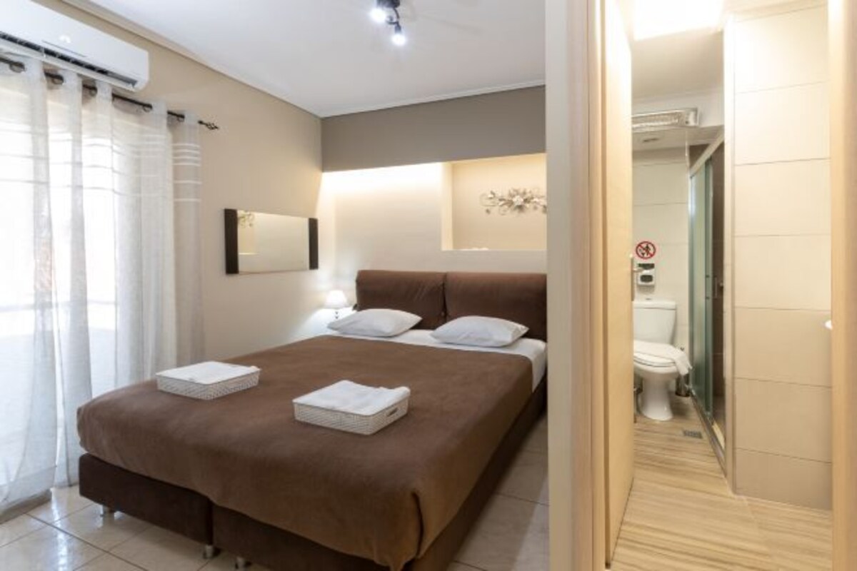 Quarto de hotel com cama, mesas de cabeceira, espelho e banheiro visível através de uma porta aberta.