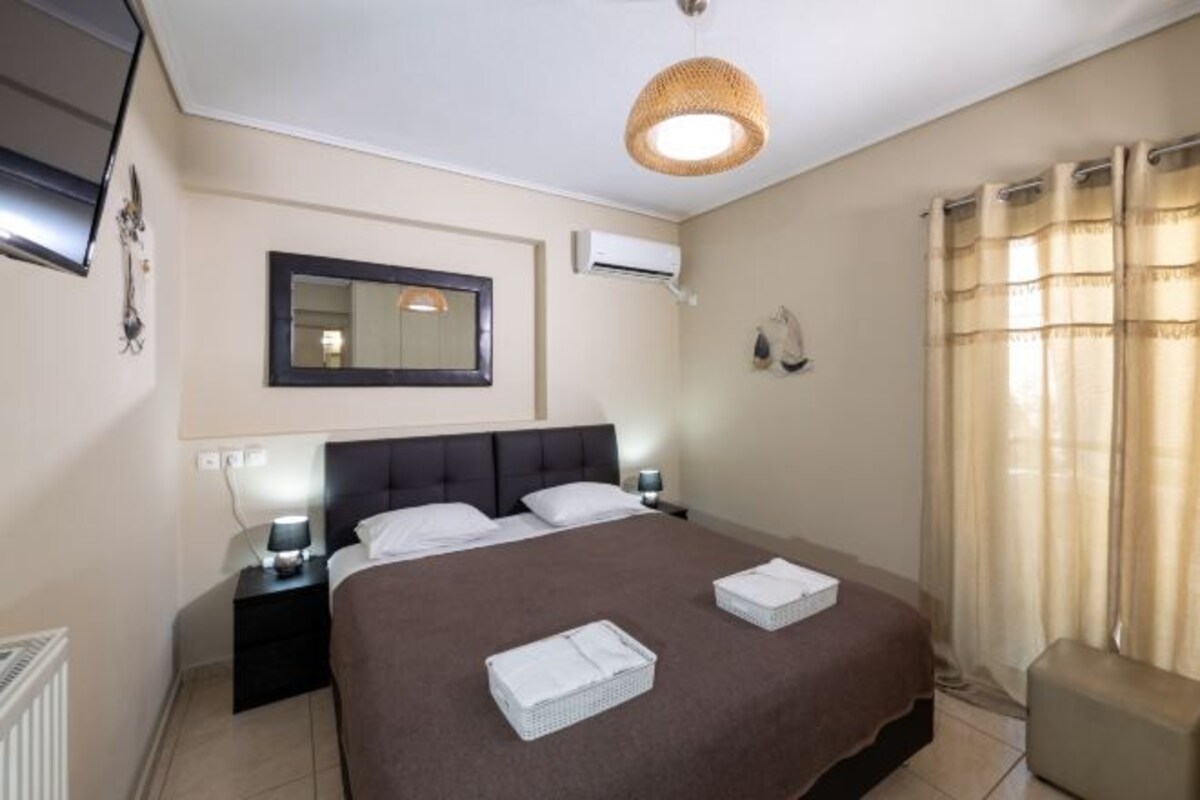 Quarto de hotel com cama, mesas de cabeceira, espelho, ar condicionado e janela com cortinas.