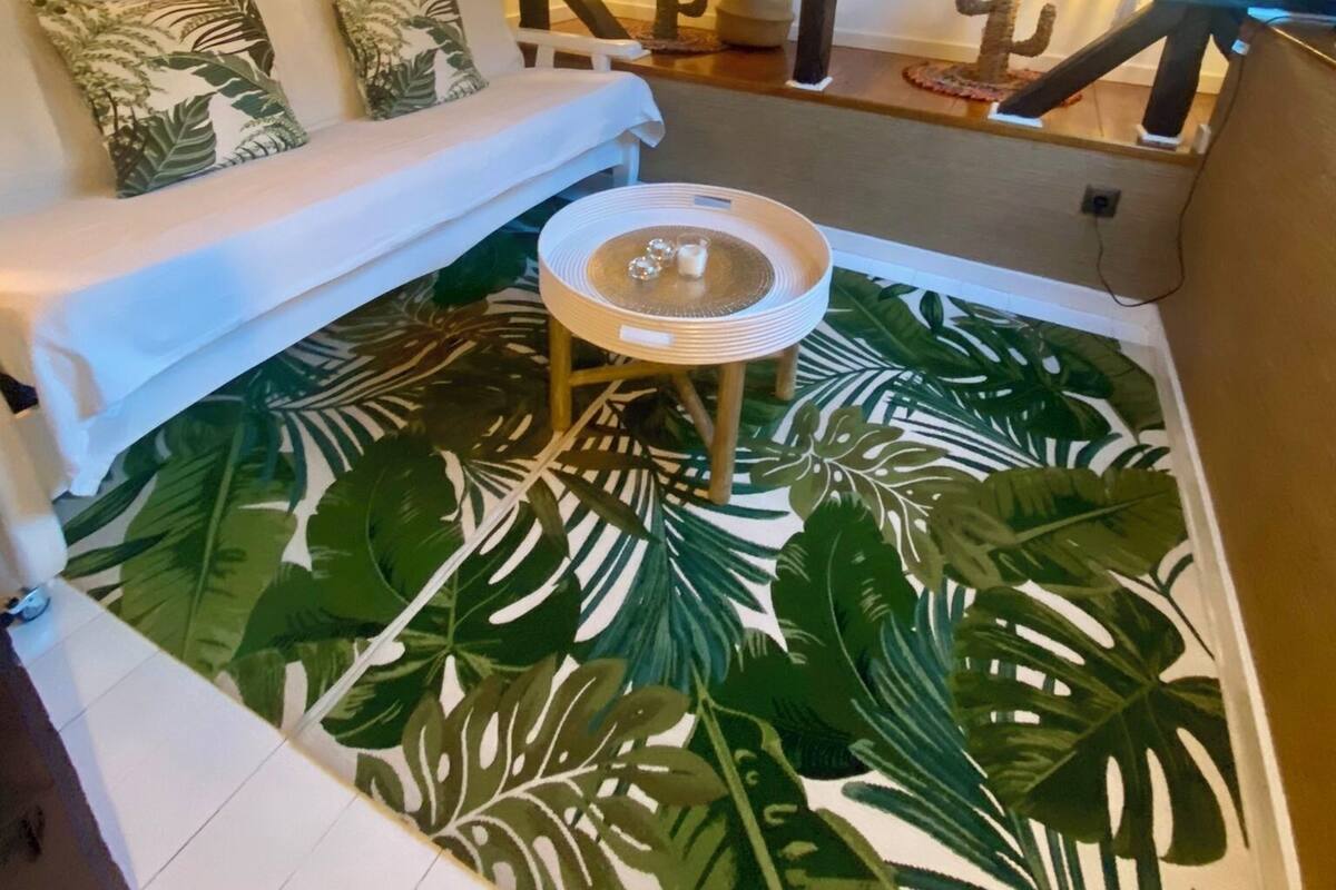 Quarto aconchegante com cama, uma pequena mesa redonda com velas e piso com padrão de folhagem tropical.