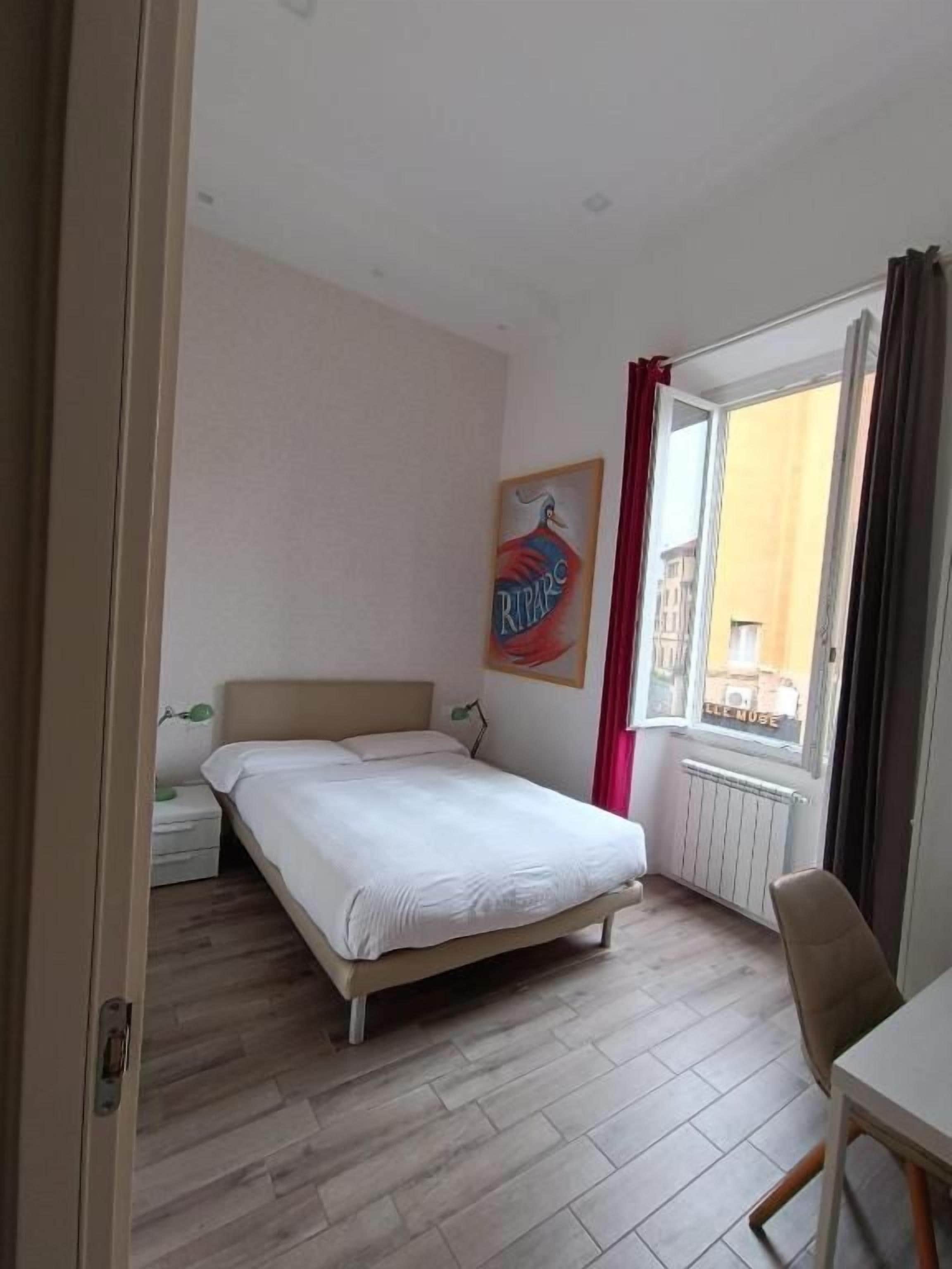 Quarto com cama, escrivaninha, cadeira, janela com cortinas e radiador.