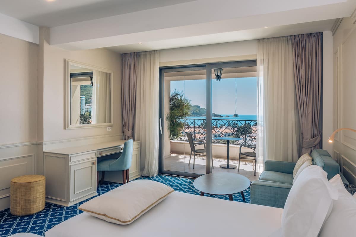 Quarto de hotel com cama, escrivaninha, cadeira, mesa pequena e varanda com vista para o mar.