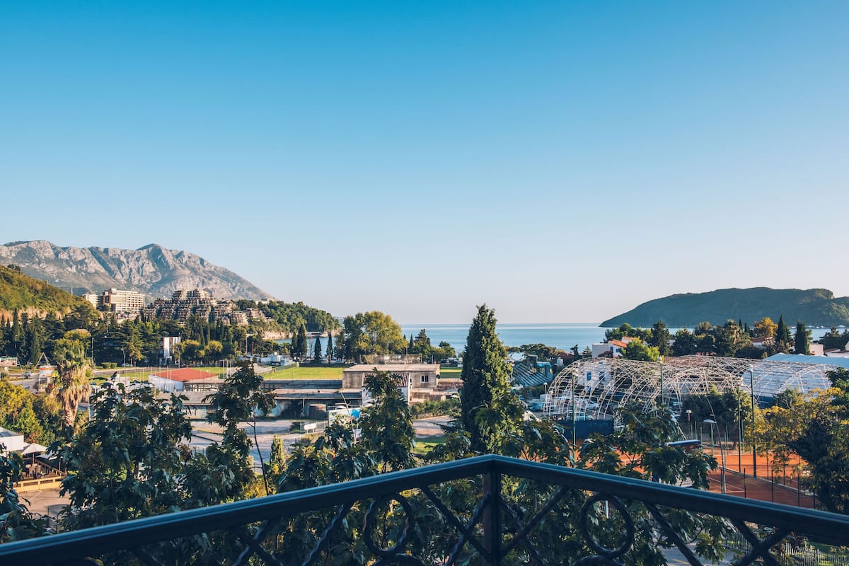 Paisagem costeira com montanhas, edifícios e um campo esportivo.