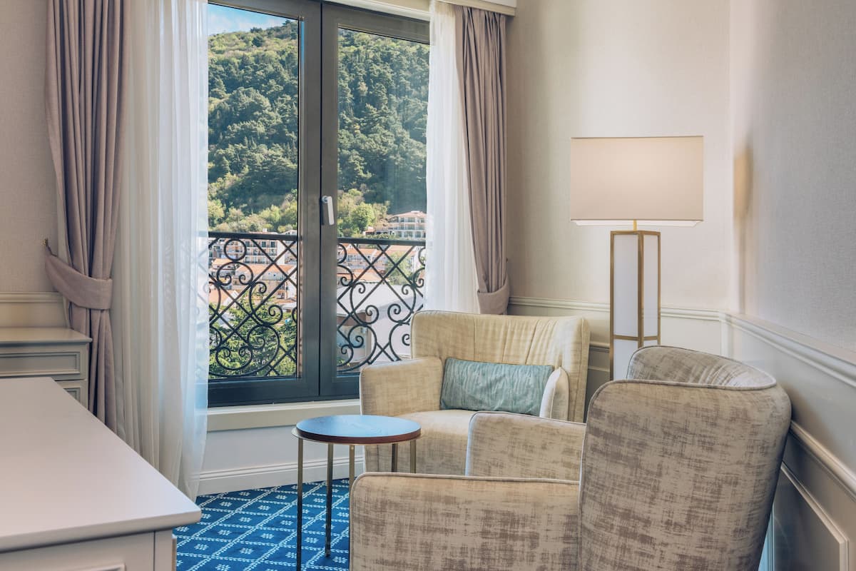 Quarto com vista para uma varanda, um sofá, uma mesa redonda pequena e um abajur.
