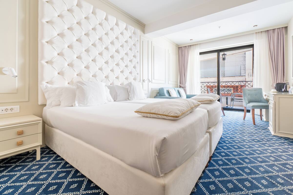 Quarto de hotel com uma cama grande, uma escrivaninha, uma cadeira e uma varanda com vista.
