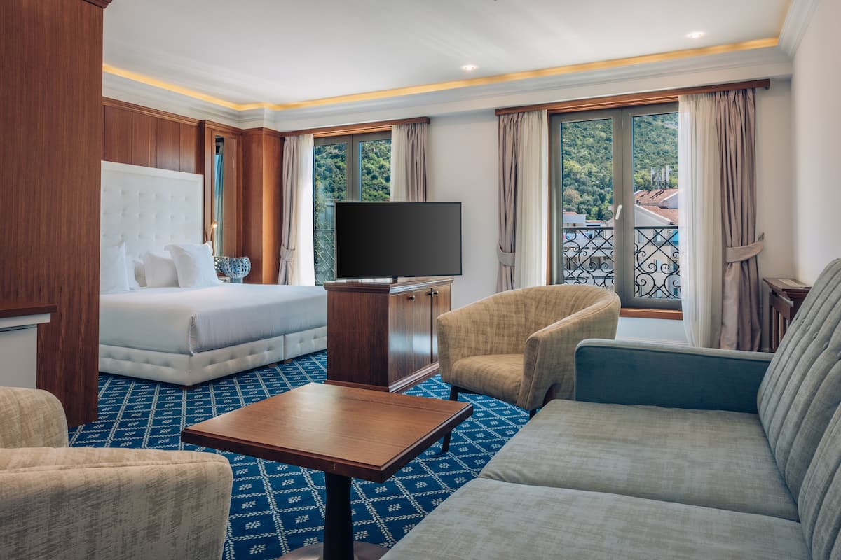 Quarto de hotel com cama, televisão, sofá e mesa de centro.