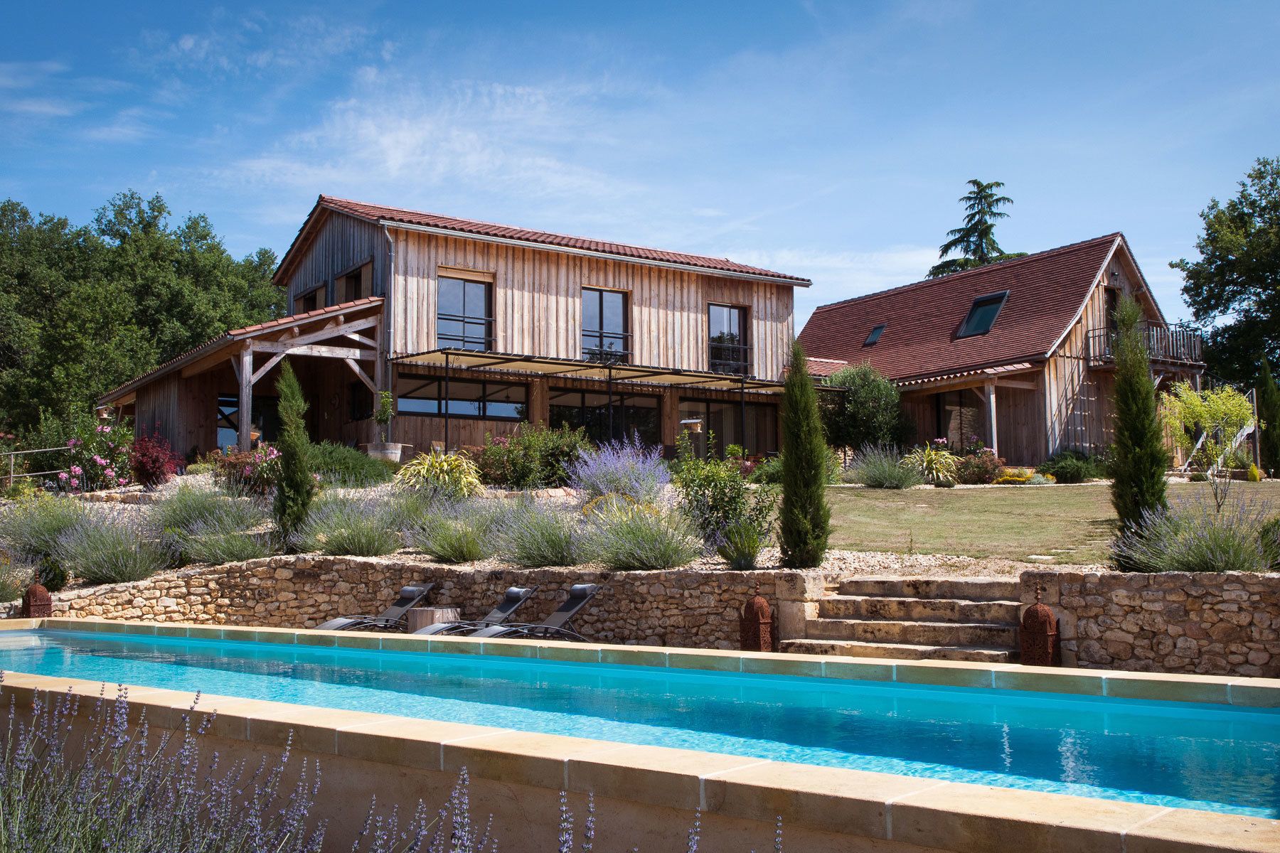 Uma casa de madeira de dois andares com uma piscina em primeiro plano.